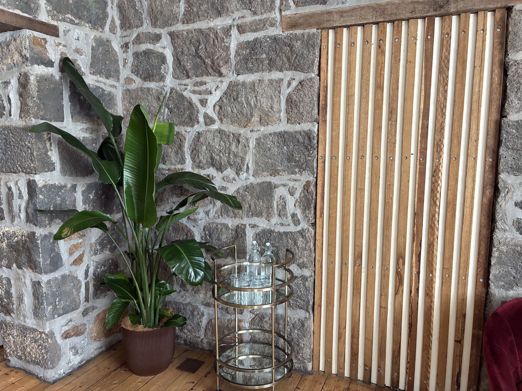 Canto com parede de pedra, planta em vaso e suporte de metal escalonado com copos.