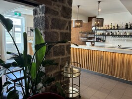 Uma área de bar com parede de pedra, balcão de madeira e diversos frascos e copos.