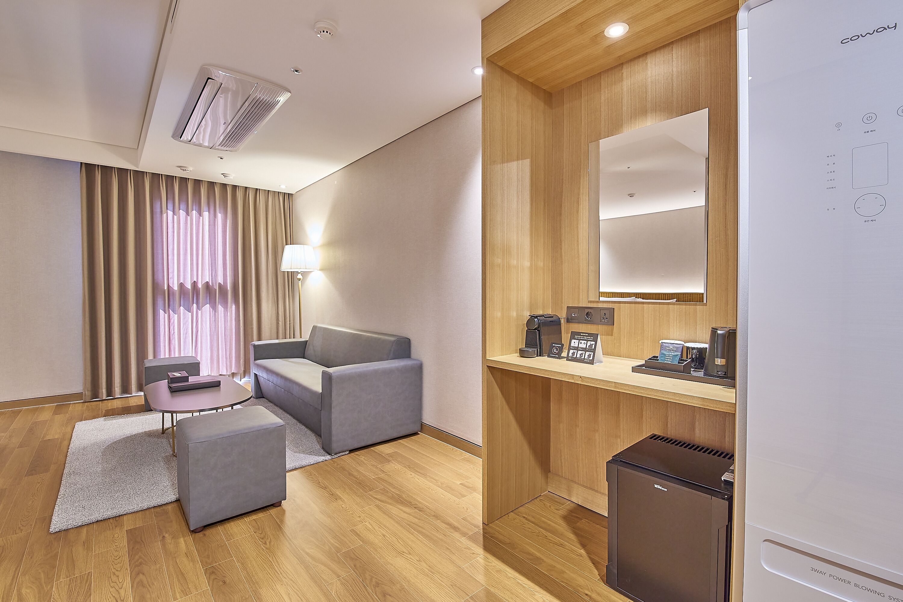 Quarto de hotel com sofá, poltrona, mesa pequena e escrivaninha com cafeteira.