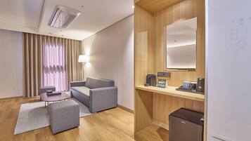 Quarto de hotel com sofá, poltrona, mesa pequena e escrivaninha com cafeteira.