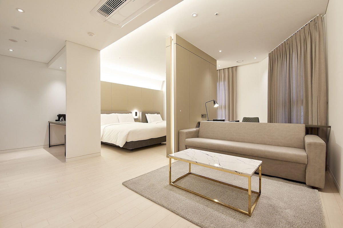 Quarto de hotel moderno com cama, sofá, mesa de centro e escrivaninha.