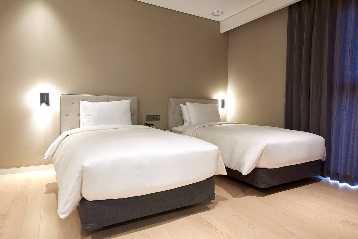 Quarto de hotel com duas camas, piso de madeira e uma janela grande com cortinas.