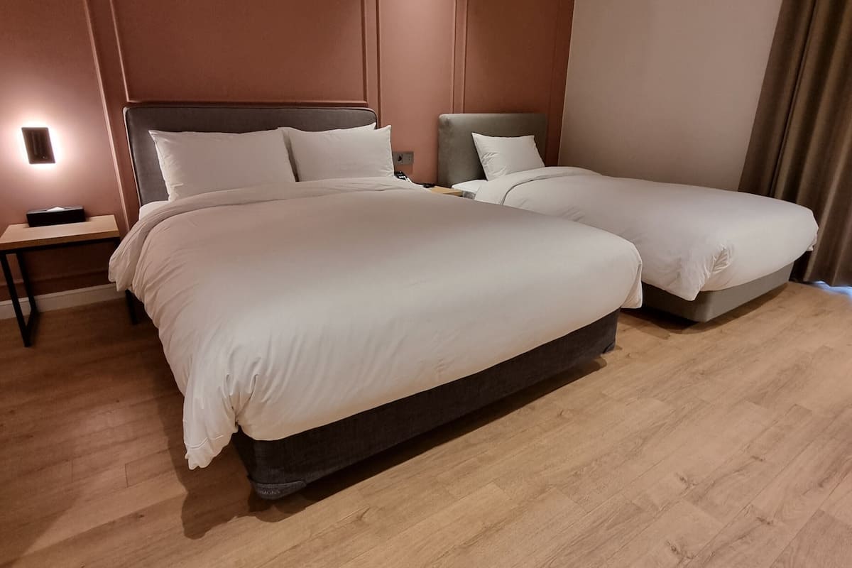 Quarto de hotel com duas camas, uma mesa de cabeceira e uma luminária fixada na parede.