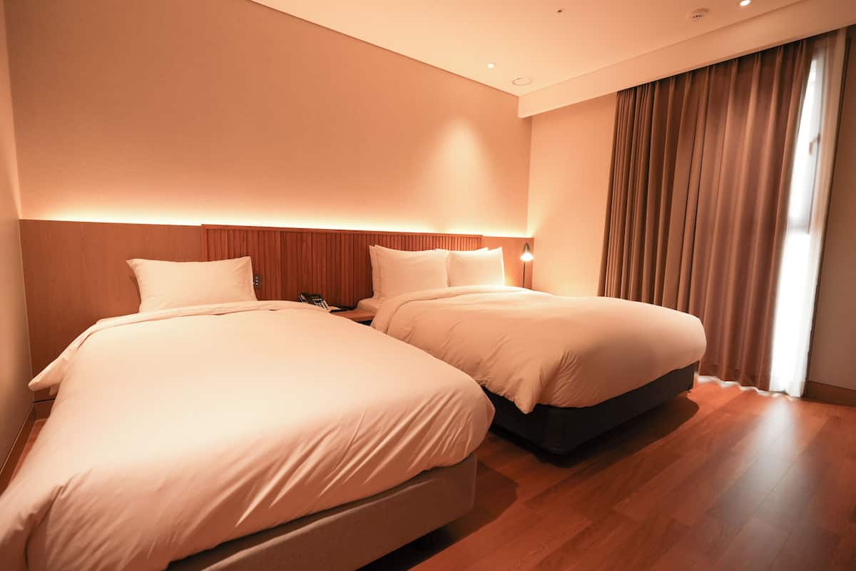 Quarto de hotel com duas camas, soalho de madeira e uma janela grande com cortinas.