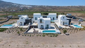 Uma villa branca moderna com várias piscinas, rodeada por um jardim bem cuidado e vista para a cidade ao longe.