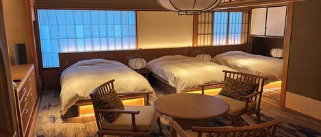 Quarto em estilo japonês tradicional, com duas camas, uma cadeira de madeira, uma mesinha e uma janela grande com vista.