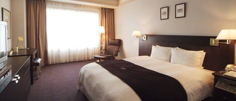Quarto de hotel com uma cama grande, duas luminárias de cabeceira, uma escrivaninha com telefone e uma cadeira.