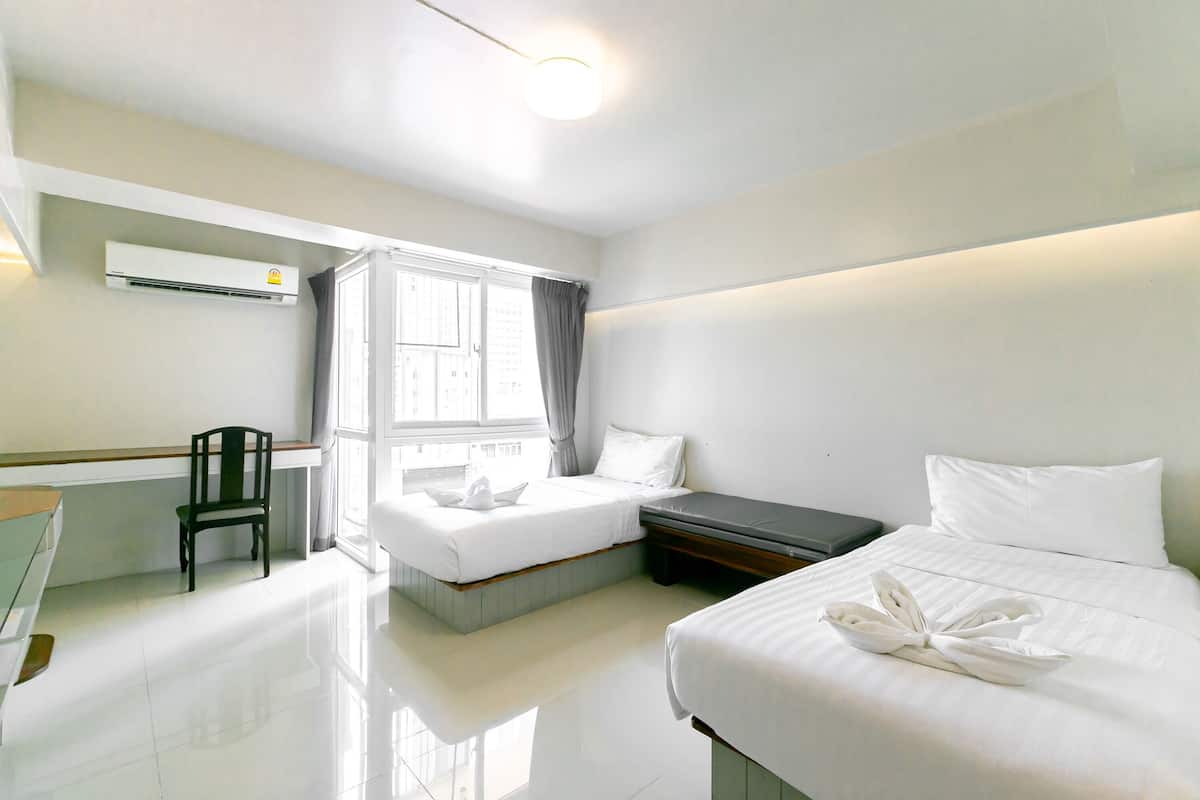 Quarto de hotel com cama, escrivaninha, cadeira e janela com cortinas.