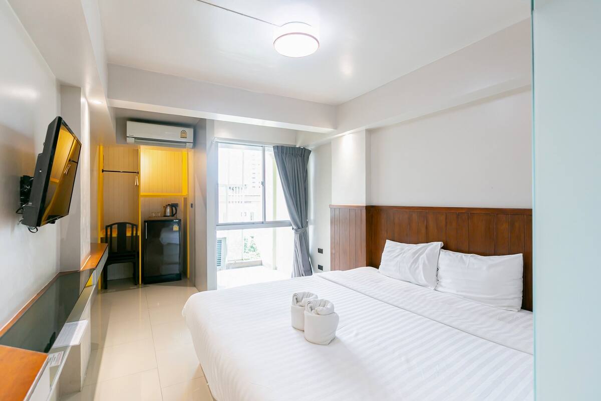 Quarto de hotel com cama, escrivaninha, televisão, ar condicionado, janela com cortinas e vista exterior.