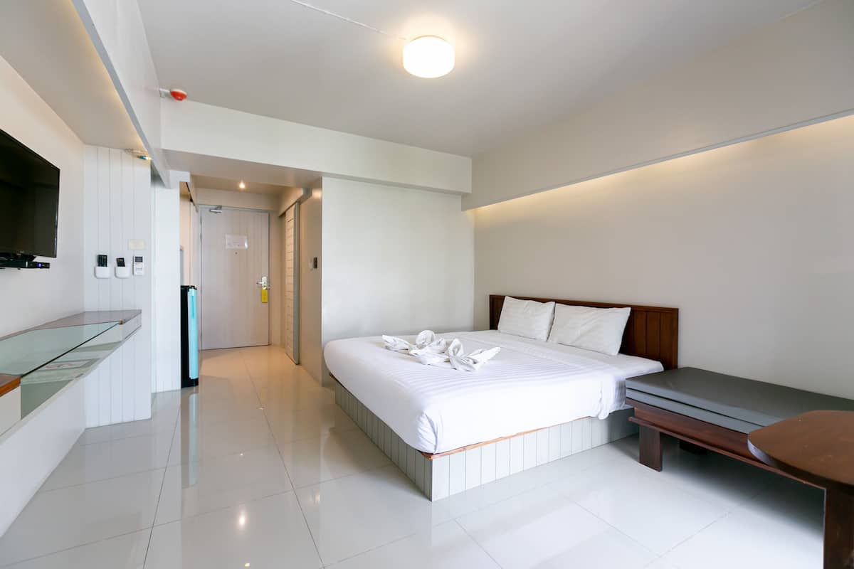 Quarto de hotel moderno com cama bem arrumada, mesa de cabeceira, televisão de tela plana e divisória de vidro.
