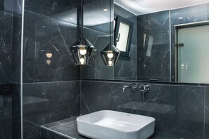 Casa de banho moderna com uma pia branca, paredes de mármore escuro e duas luzes pendentes.