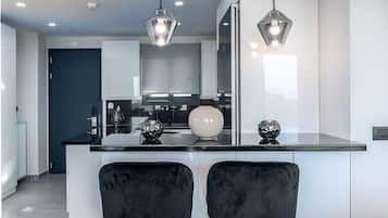 Uma cozinha moderna com uma ilha central, duas cadeiras pretas estilo bar e iluminação pendente.