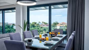 Uma zona de refeições moderna com mesa de vidro, cadeiras cinzentas e vista para a cidade através de grandes janelas.