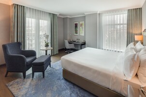 Quarto de hotel com uma cama grande, uma escrivaninha, uma cadeira e uma pequena mesa com uma planta.