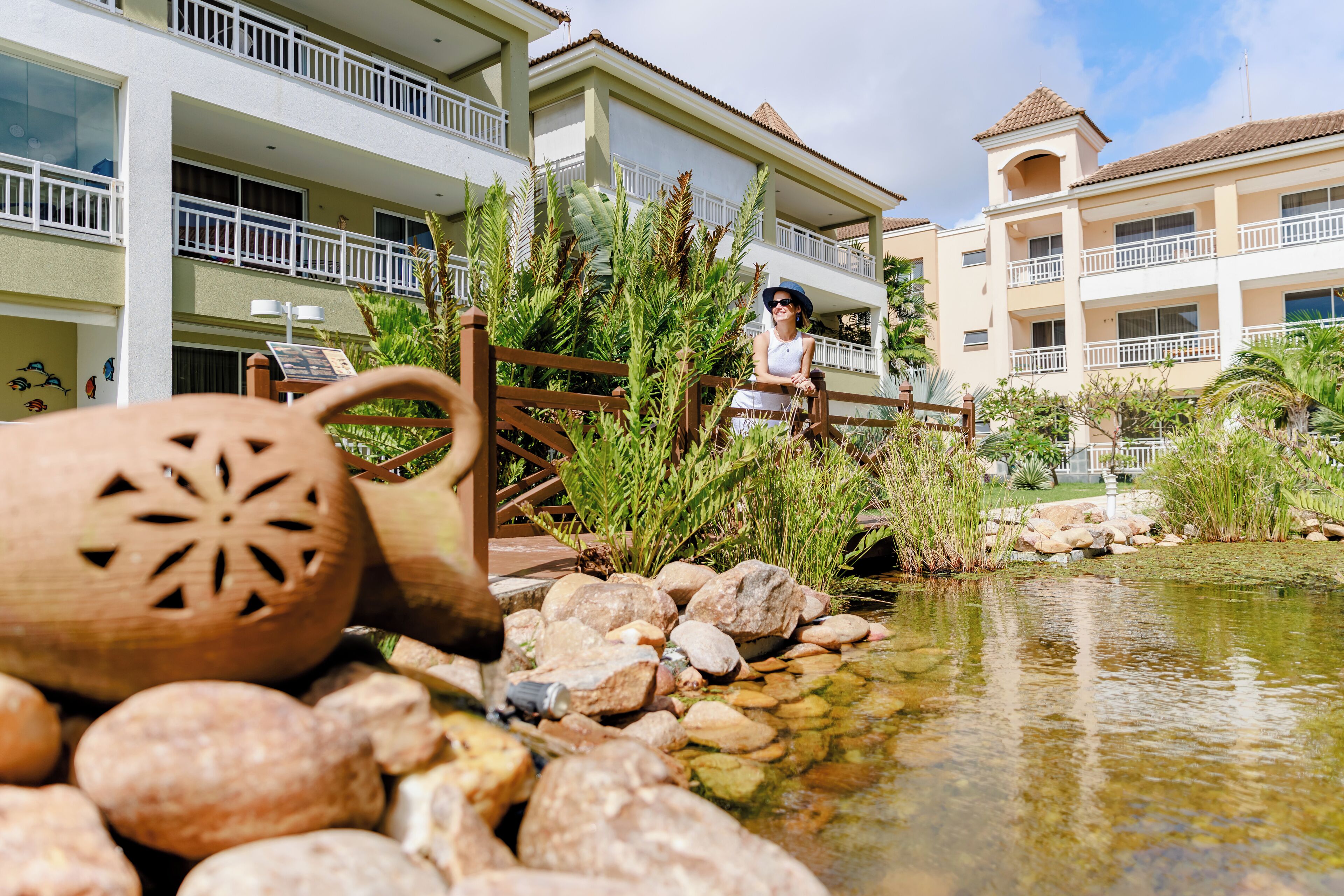 Um hotel com piscina, uma ponte de madeira e uma pessoa sentada sobre a ponte.