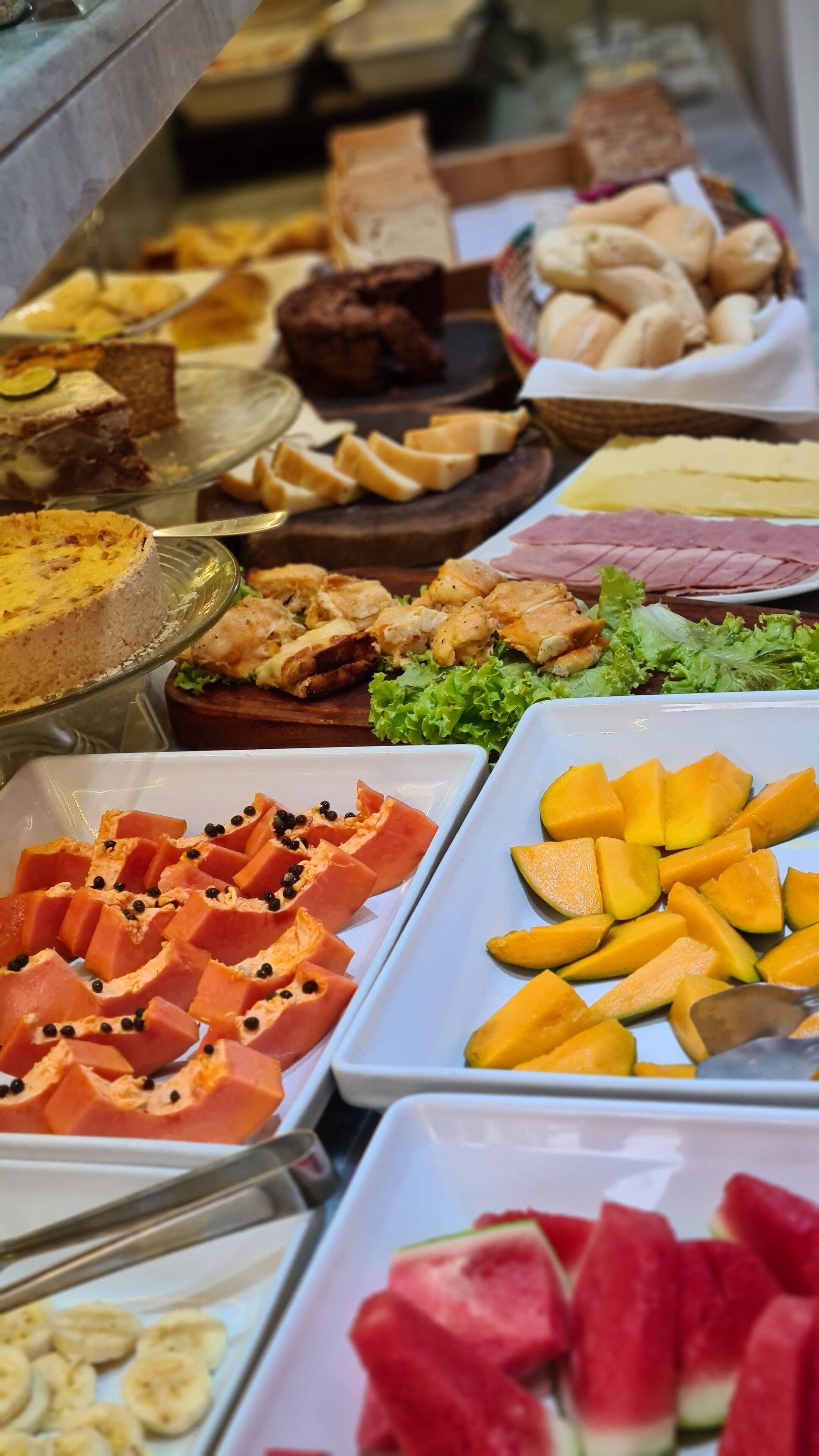 Buffet com diversos alimentos, incluindo frutas, vegetais e diferentes tipos de pão.