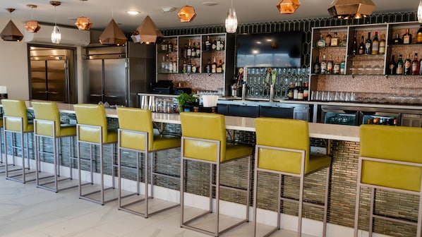 Uma área de bar com um balcão comprido, diversas prateleiras cheias de garrafas de bebidas e uma tela de televisão.
