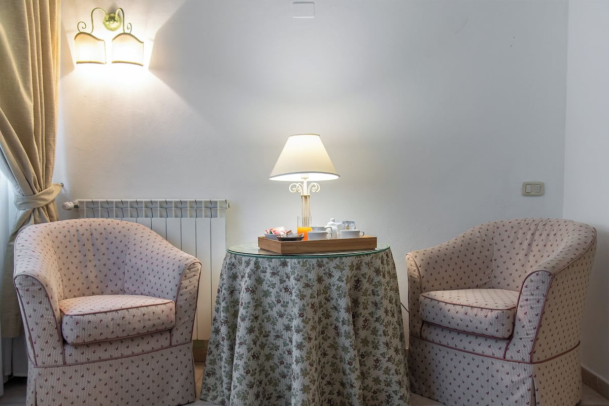 Quarto com duas poltronas, uma mesa com toalha de mesa florida e um abajur.