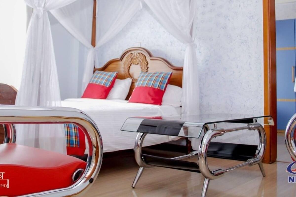 Quarto com cama de dossel, mesa de cabeceira e uma cadeira vermelha.