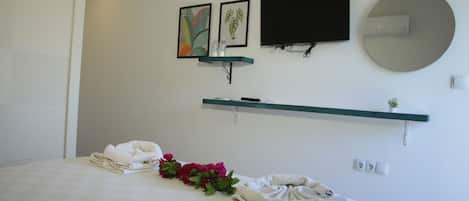 Quarto de hotel com cama, toalhas, um buquê de flores, televisão e obras de arte penduradas na parede.