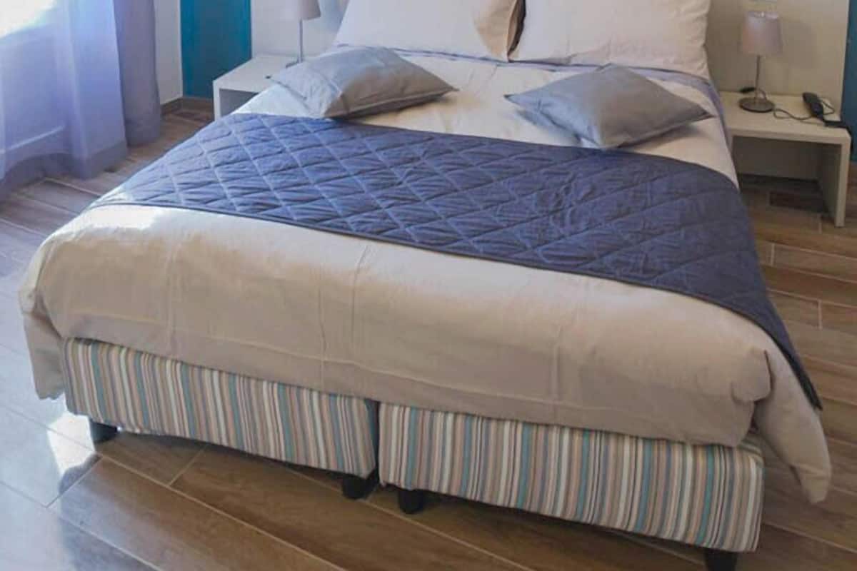 Cama bem arrumada com cobertura acolchoada e almofadas listradas, luminária de cabeceira e mesa de cabeceira com abajur.