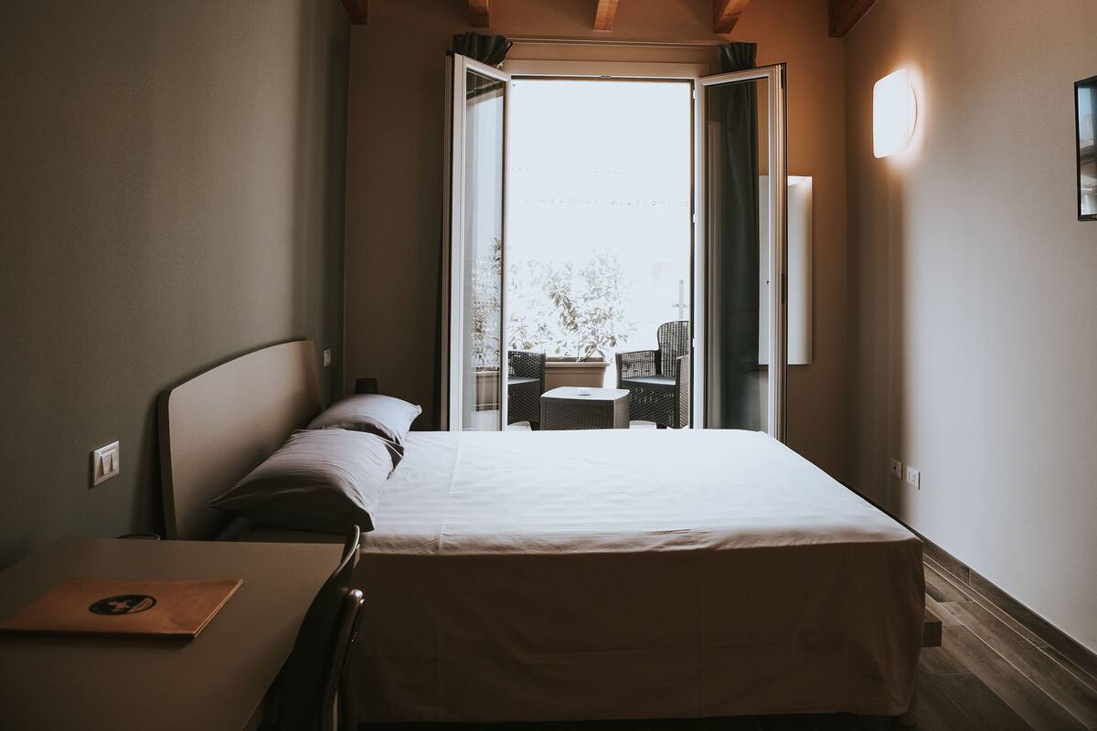 Quarto com teto de madeira, uma cama, uma escrivaninha e janela com vista para o exterior.