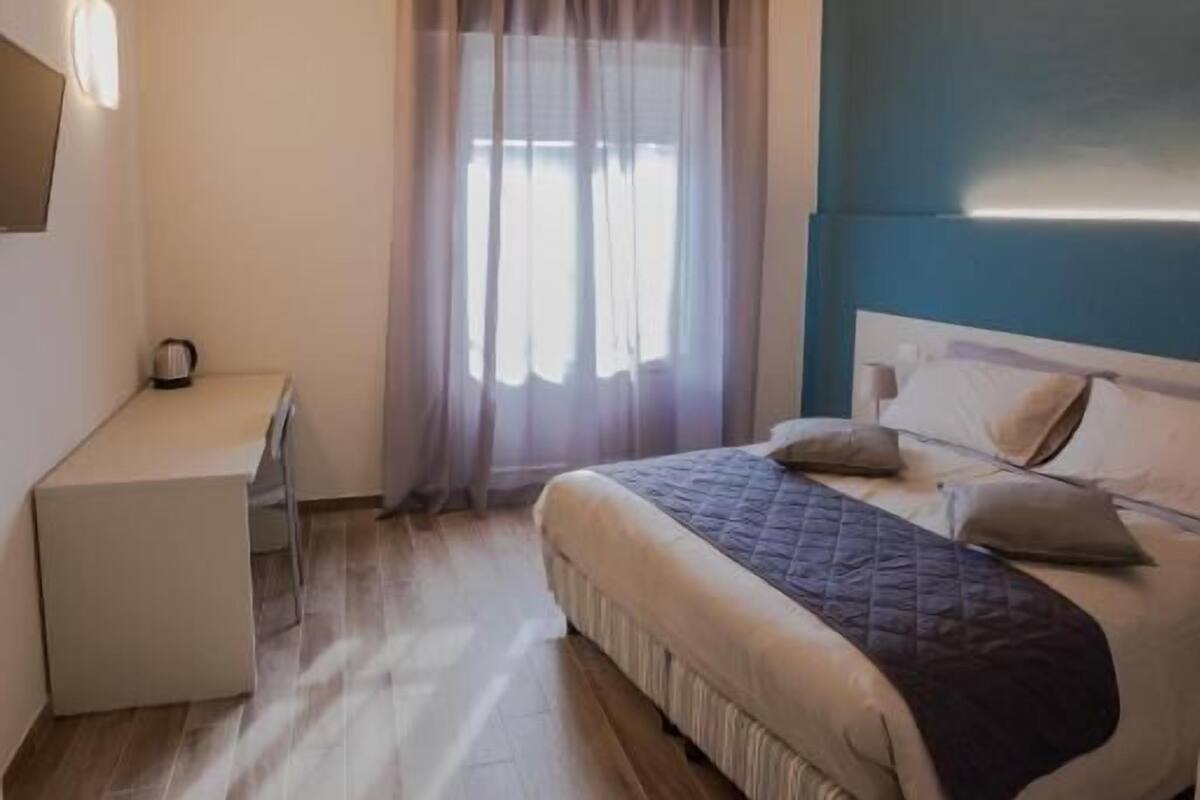 Quarto de hotel moderno com cama, escrivaninha e janela com cortinas.