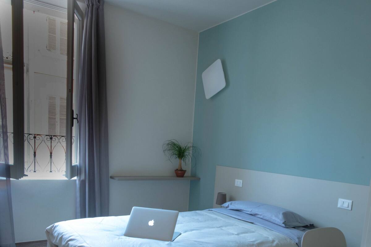 Quarto bem arrumado com uma cama, um laptop, uma mesa de cabeceira e um vaso de planta.