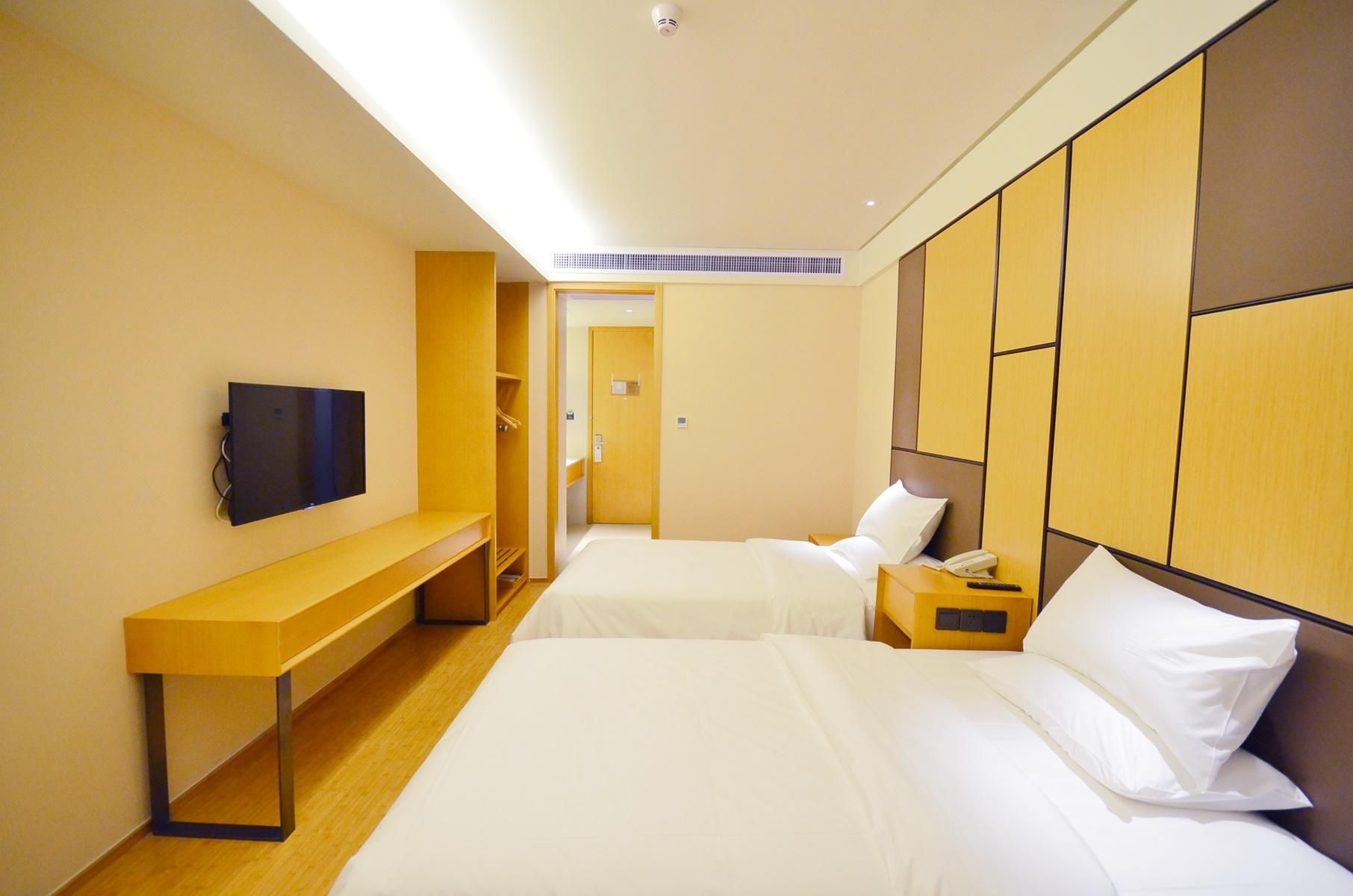 Quarto de hotel com duas camas, televisão, escrivaninha e guarda-roupa.