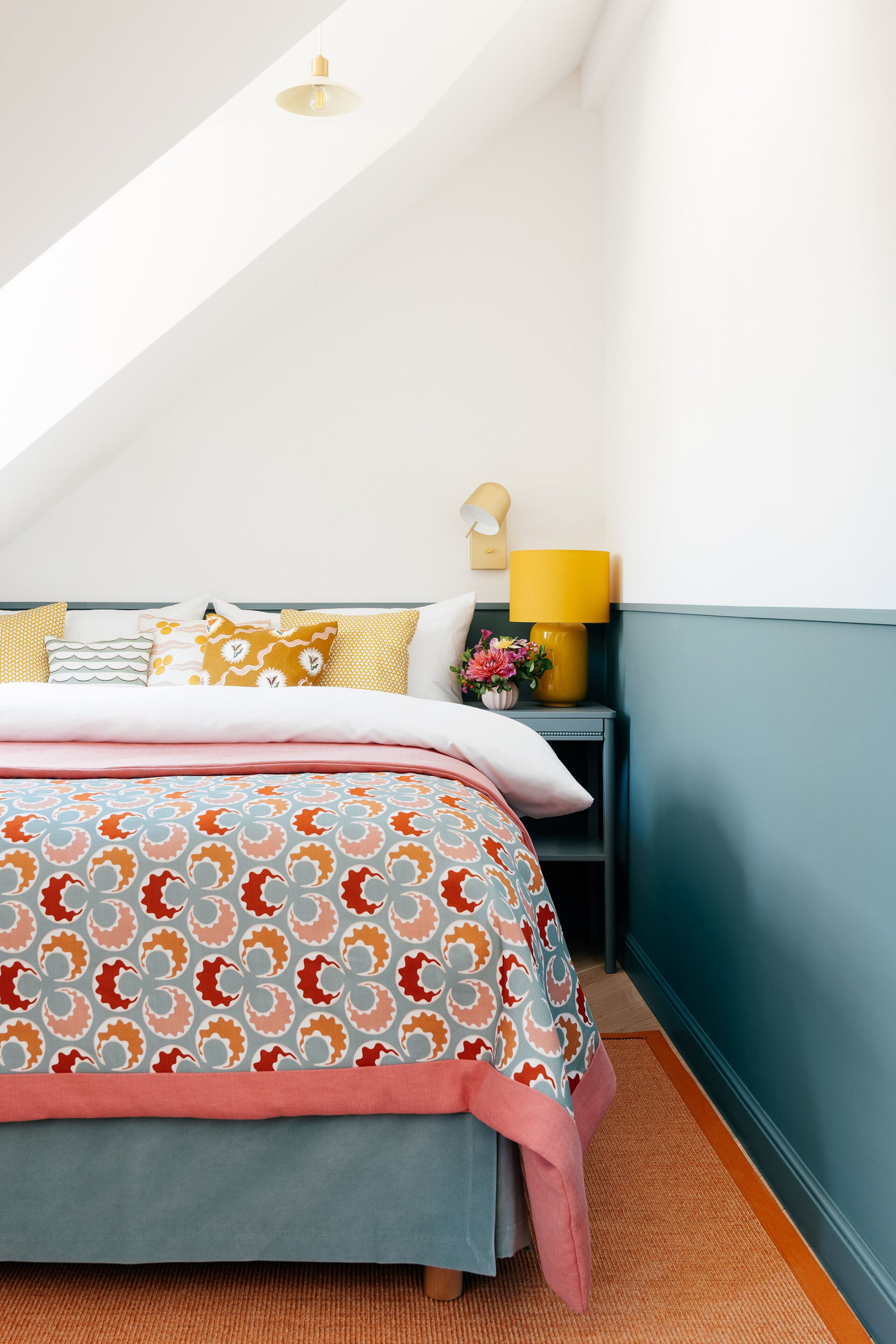 Quarto com cama, mesa de cabeceira, luminária e prateleira na parede.