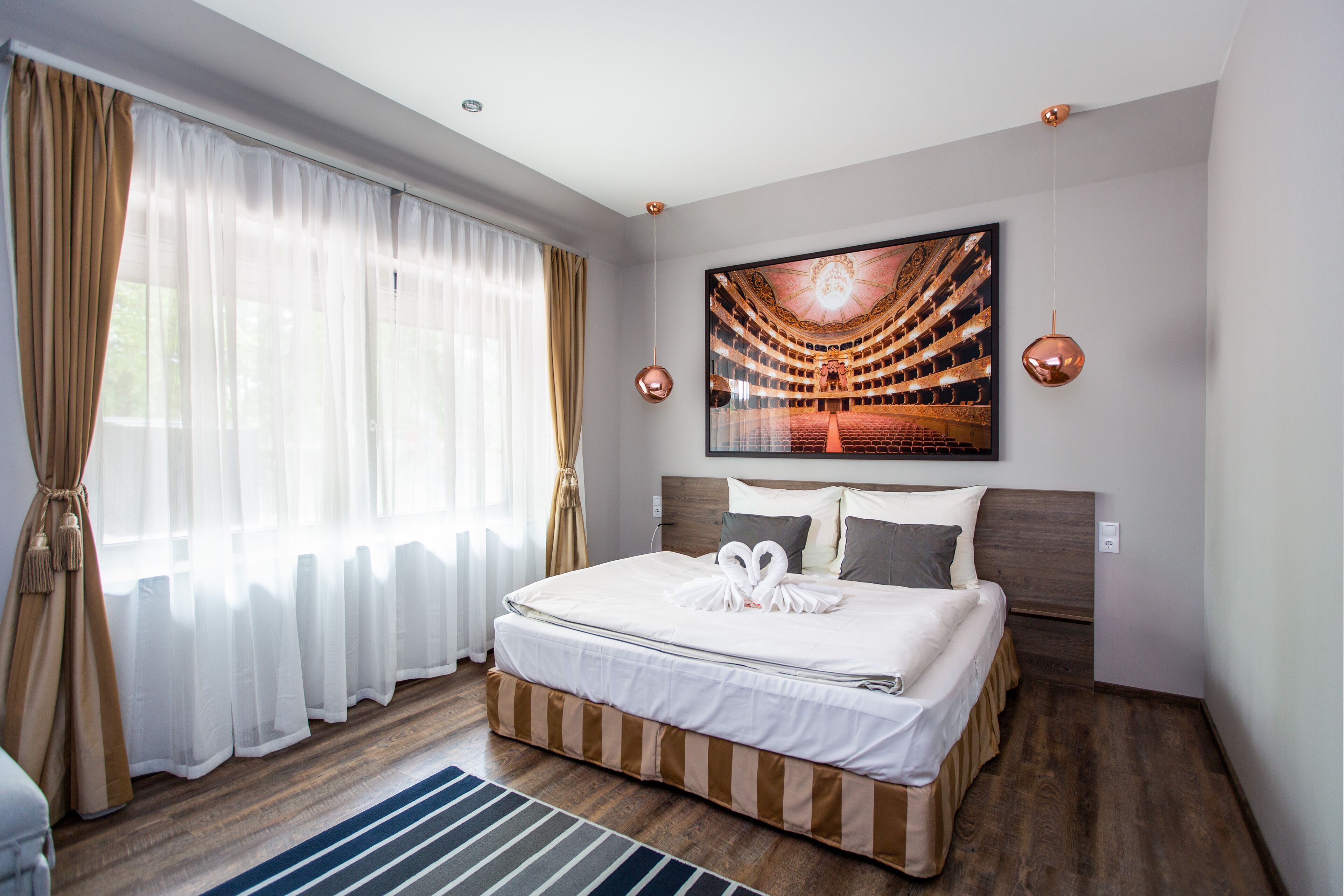 Quarto de hotel com uma cama grande, vista do teto de um teatro e um lustre moderno.