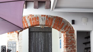 Uma área externa com assentos, um arco de tijolos, um balcão de bar e piso ladrilhado.