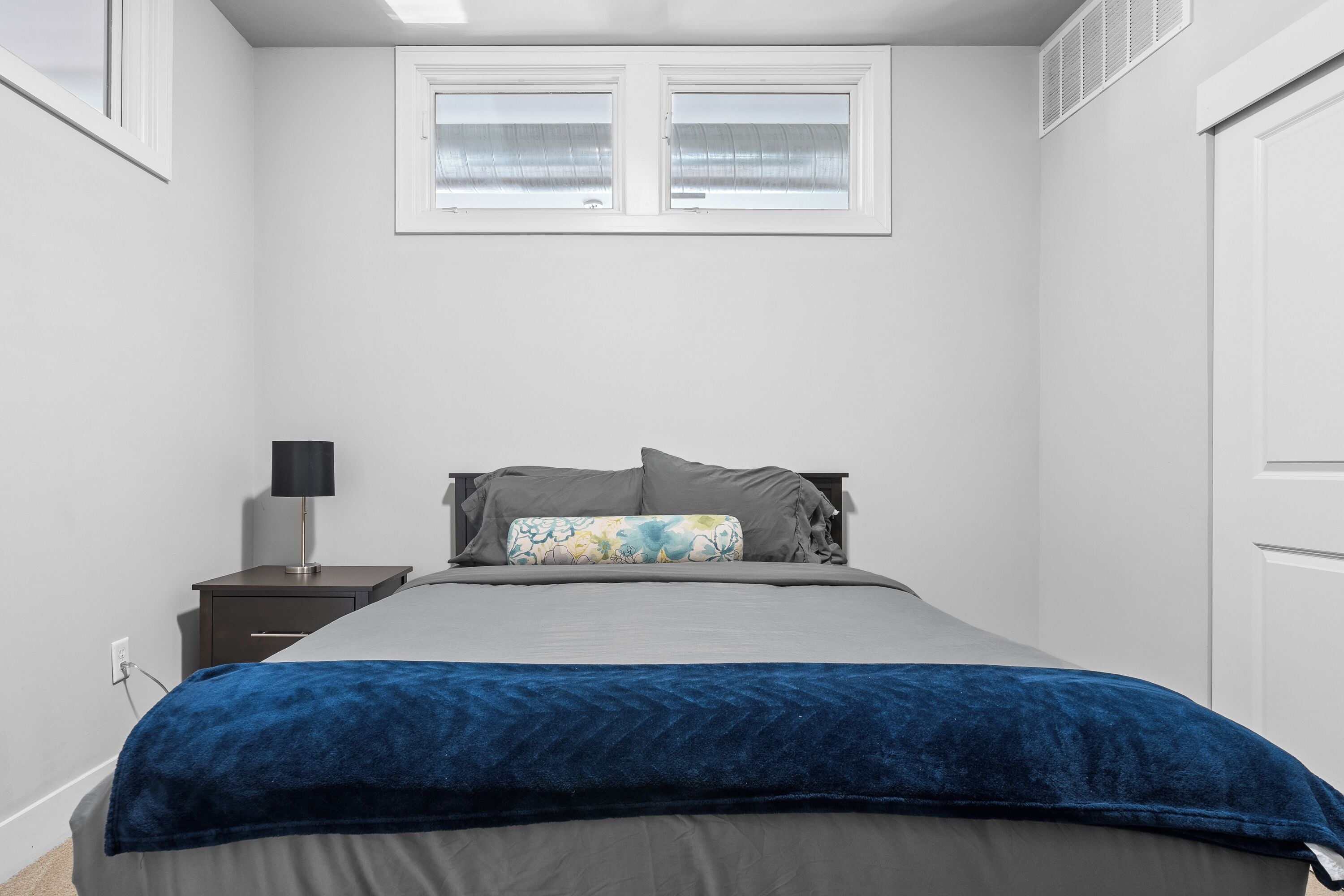 Um quarto com uma cama, uma mesinha de cabeceira, uma luminária e uma janela.