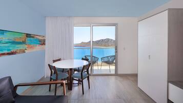 Quarto moderno com mesa de jantar e cadeiras, um sofá e uma janela grande com vista para o mar e montanhas.