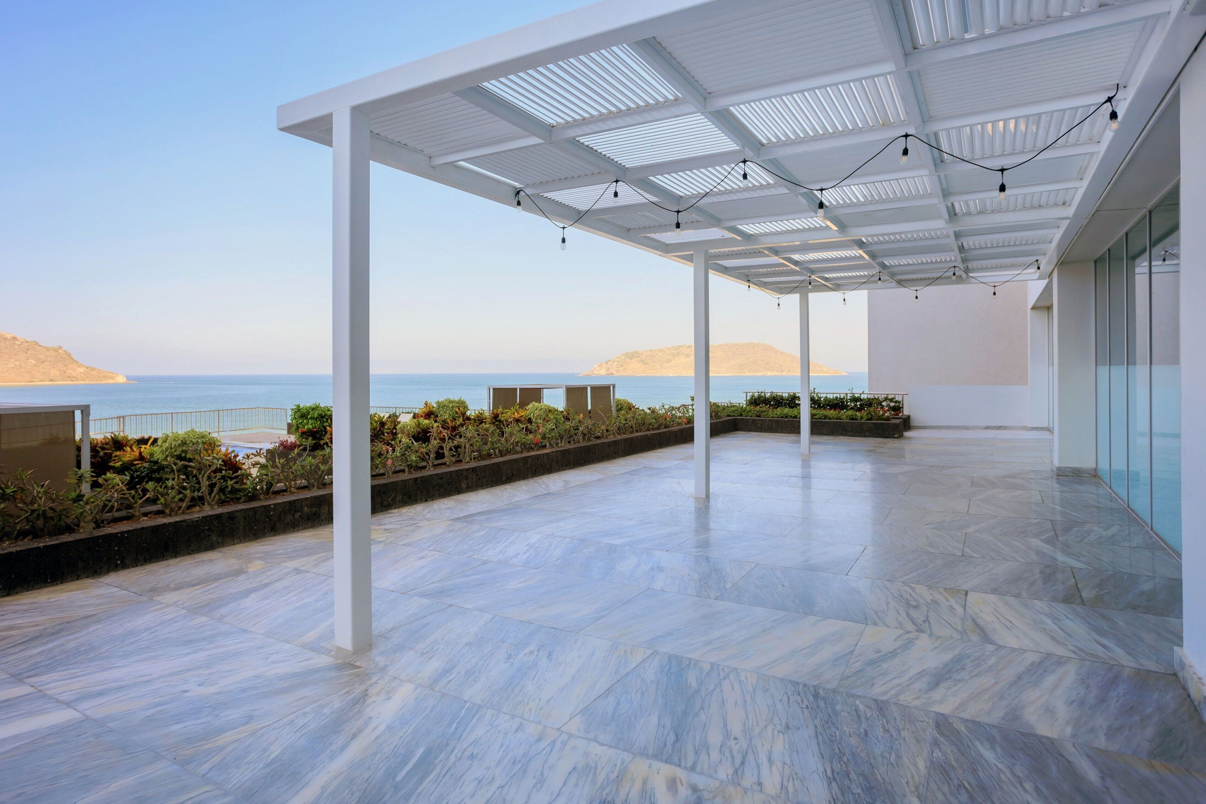 Um terraço espaçoso com vista para o mar, com pérgula branca e soalho em azulejos.