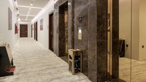 Corredor moderno de hotel com piso de mármore, obras de arte emolduradas e uma coluna de mármore.