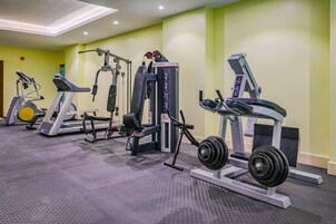 Uma academia com diversos equipamentos de exercícios, incluindo esteiras, aparelhos de musculação e um banco de imprensa.