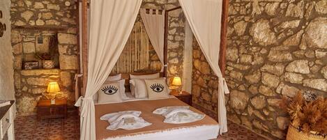 Quarto tradicional com paredes de pedra, cama de dossel, lustre e cesta de vime.