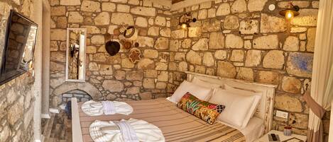 Quarto com paredes de pedra, uma cama, mesas de cabeceira e um espelho.