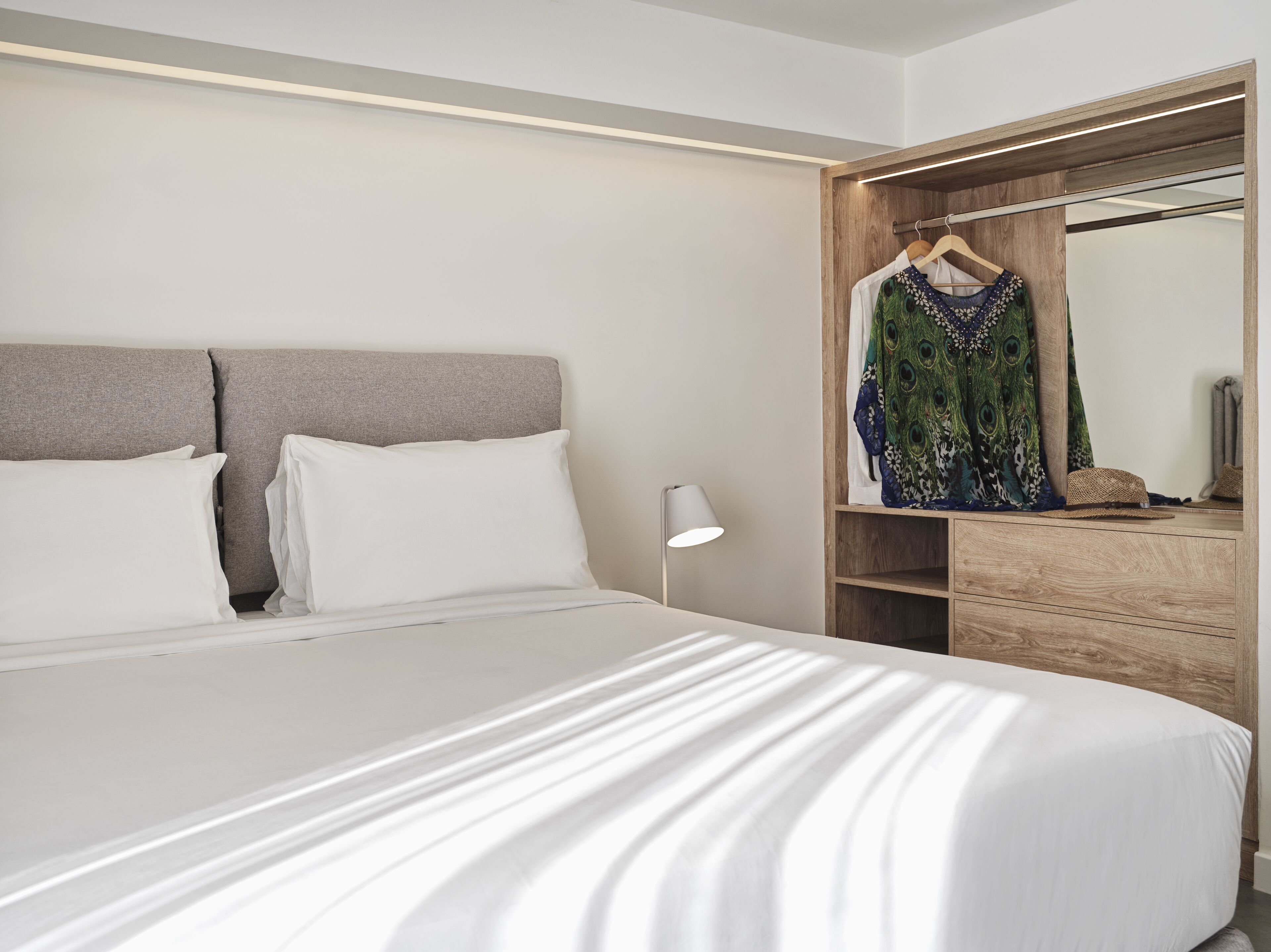 Quarto de hotel moderno com uma cama grande, cômoda de madeira, espelho e cabides.