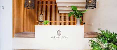 Uma área de recepção com balcão branco, ripas de madeira e luminárias pendentes pretas.