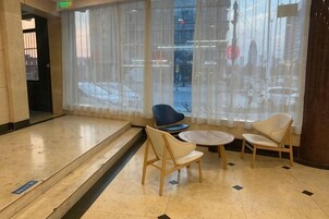 Um saguão de hotel com área de estar, janelas amplas e vista para a rua.