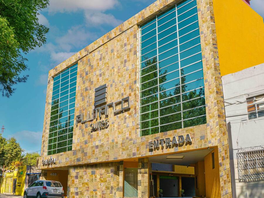 Um hotel com uma fachada de vidro ampla, exterior amarelo e bege, e uma placa indicando a entrada.