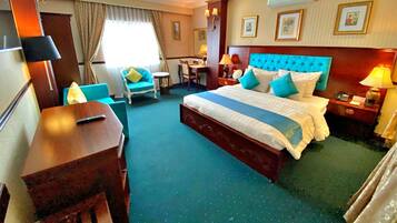 Quarto de hotel com uma cama grande, uma escrivaninha, uma cadeira e uma pequena mesa.