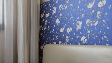 Uma cama com roupa de cama branca, cabeceira floral azul e cortinas finas.
