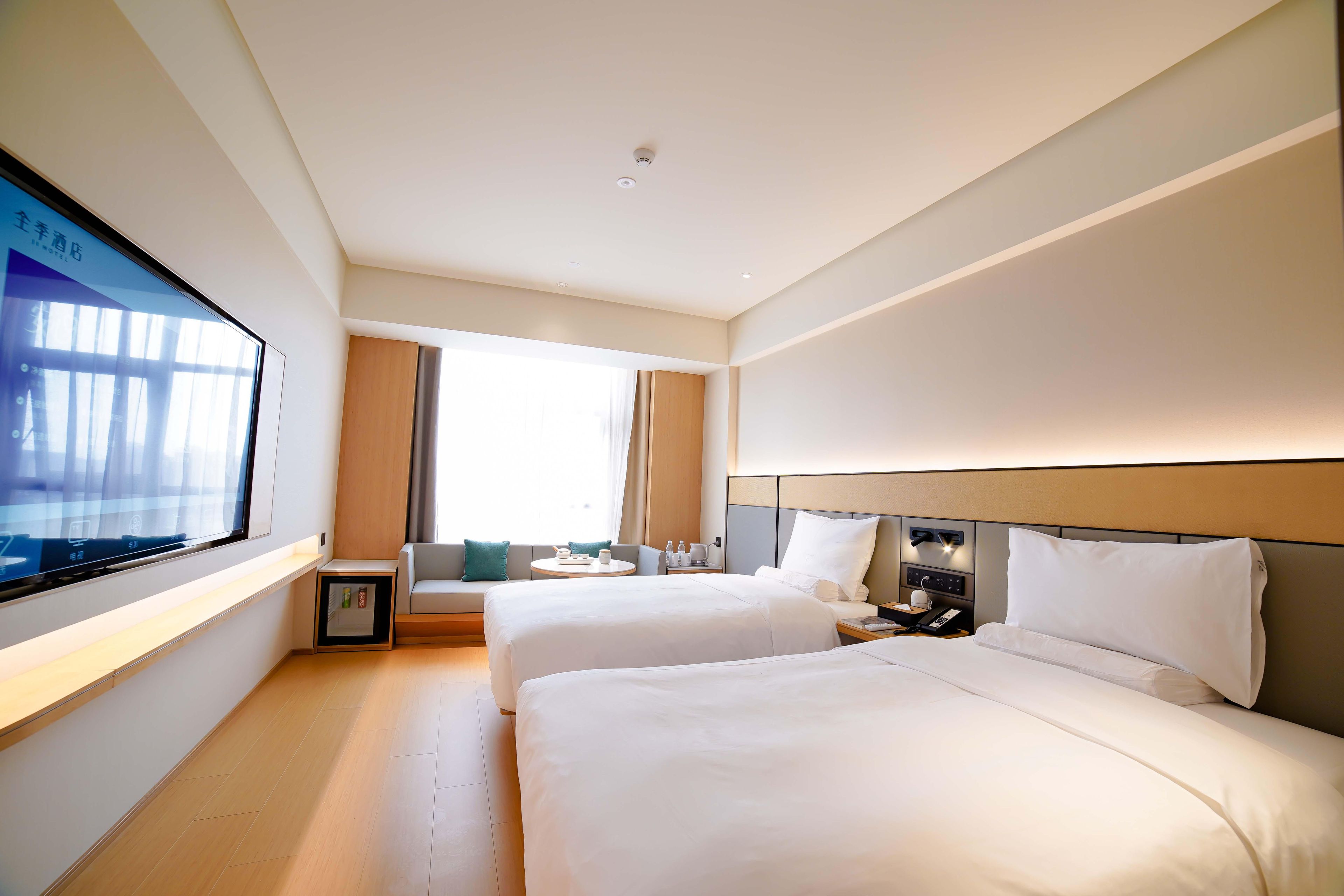 Quarto de hotel com duas camas, televisão, mesa pequena e sofá.