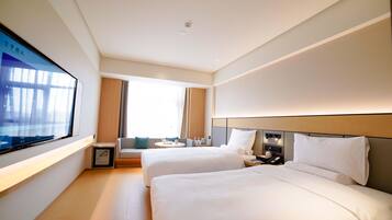 Quarto de hotel com duas camas, televisão, mesa pequena e sofá.