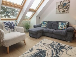 Uma sala de estar no estilo loft com sofá seccional, uma poltrona, uma janela ampla e um ventilador de teto.