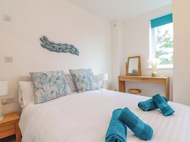Quarto de hotel com cama, mesa de cabeceira, escrivaninha com espelho e janela.