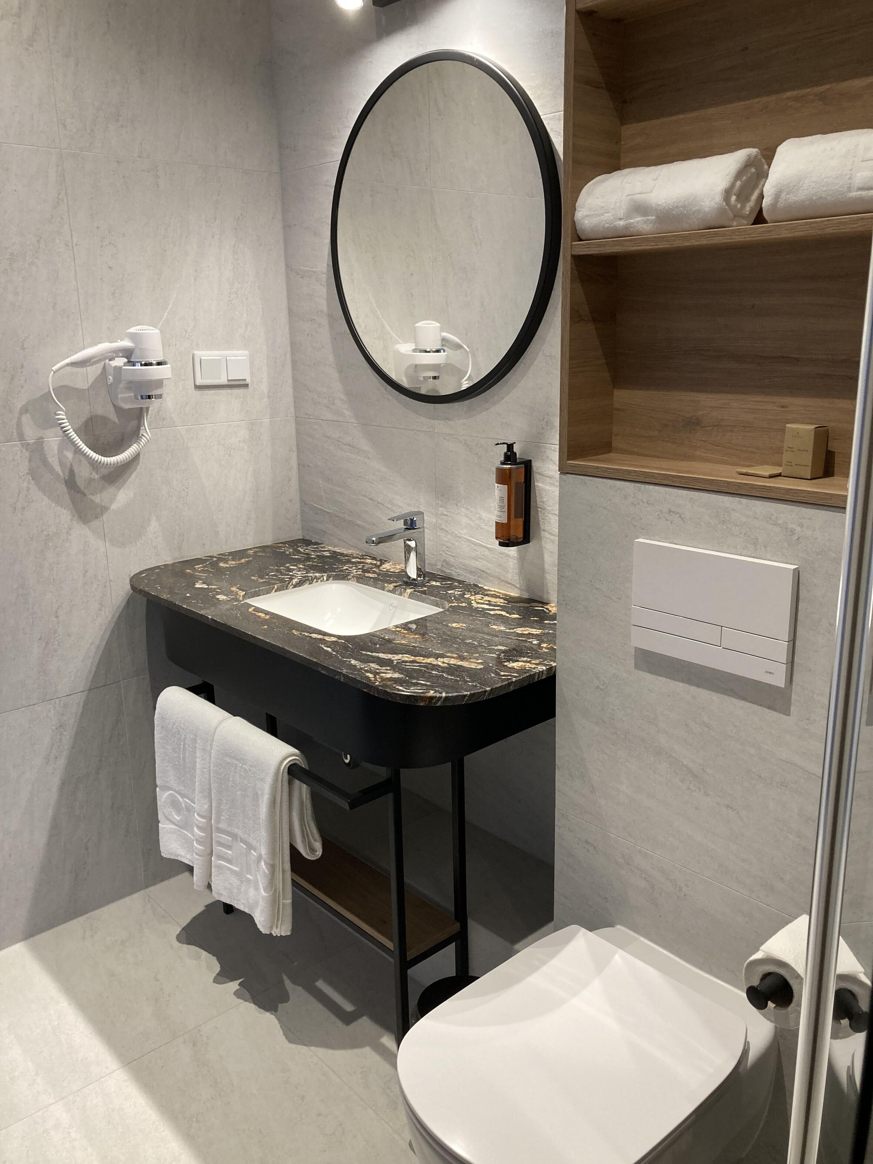 Um banheiro moderno com pia de mármore, um espelho redondo, porta-toalhas e vaso sanitário.